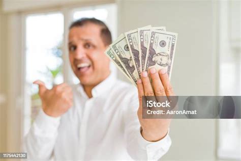 중년 남자 들고 달러의 무리를 가리키는 하 고 행복 한 얼굴 미소와 함께 측면에 엄지 손가락으로 표시 가리키기에 대한 스톡 사진 및 기타 이미지 Istock