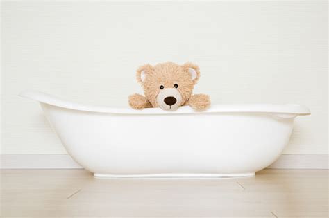 밝은 회색 벽 배경에 나무 바닥에 있는 집 방에서 흰색 플라스틱 욕조에서 보고 있는 웃는 갈색 테디 베어 근접 촬영 아기 목욕