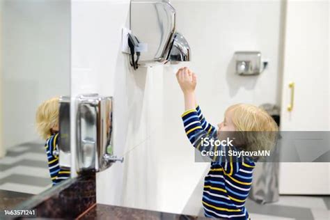 화장실을 사용하고 있는 아이 어린 소년은 자동 건조기로 화장실에서 손을 말립니다 공공 장소에서 어린이의 위생을 돌 봅니다 건강한 습관 4 5세에 대한 스톡 사진 및 기타