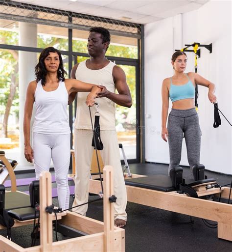 African American Man Helps Women To Exercise On Simulators During Pilates Class Stock Image