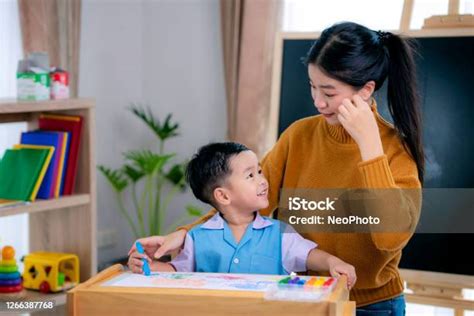 유치원에 교실에서 아시아 교사는 백보르 배경테이블에 색 연필로 종이에 그림을 그녀의 학생을 가르친다 교습에 대한 스톡 사진 및
