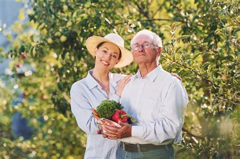 Sonriendo y sosteniendo verduras la hija está con su padre mayor en el jardín durante el día