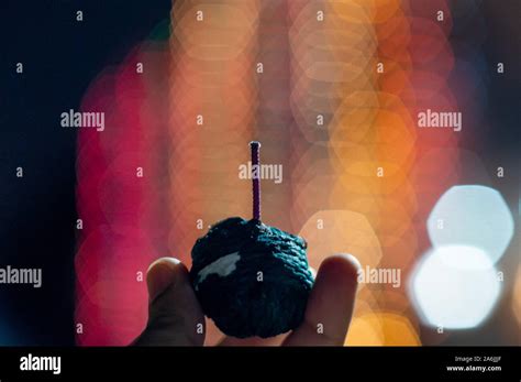 Human Hand Holding Green Sutli Rassi Bomb In Front Of Out Of Focus Lights With A Hexagon Bokeh