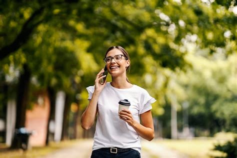 Uma universitária feliz está de pé no campus e conversando por telefone com colegas Foto Premium