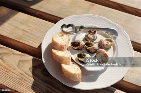 달팽이 껍질이 있는 요리는 다양한 소스 페스토 트러플 치즈 프렌치 바게트 조각 껍질 포크 야외 카페의 나무 테이블과 함께 흰색 클래식 접시에 담겨 제공됩니다 0명에 대한