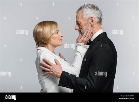 Side View Of Mature Bride Touching Face Of Groom In Suit Isolated On