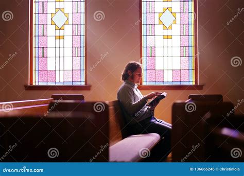 Christian Man Sitting Alone In Dark Empty Church Pew By Bright Stained