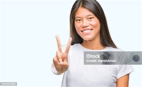 승리 표시를 하 고 카메라에 윙크 하는 행복 한 얼굴로 웃 고 고립 된 배경 위에 젊은 아시아 여자 번호 2입니다 긍정적인 감정