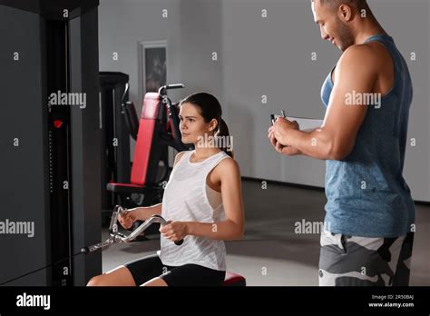 Trainer Writing Down Plan Of Workouts While Woman Doing Exercise In Modern Gym Stock Photo Alamy