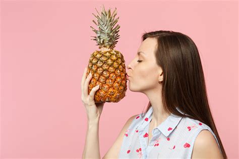 여름 옷에 젊은 여자의 측면 보기 스튜디오에서 분홍색 파스텔 벽 배경에 고립 된 신선한 잘 익은 파인애플 과일 키스를 개최