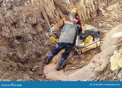 A Worker Compacts Soil Or Sand With A Vibrating Plate In A Trench At A