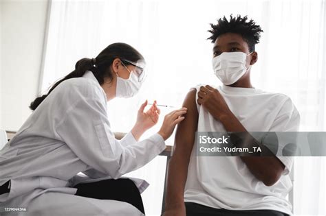 마스크와 얼굴 방패를 착용한 여성 의사 또는 간호사가 예방 접종을 위해 아프리카계 미국인 남성의 어깨에 코로나바이러스 19