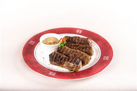 Mici 전통적인 루마니아어 고기 롤 겨자와 함께 녹색 및 빨강 잎으로 장식 백색과 빨강 접시 밝은 배경에 배치 가공육에 대한