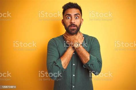 고립 된 흰색 배경 위에 서있는 우아한 셔츠를 입은 젊은 인도 사업가가 고통스러운 목졸림 때문에 외치고 질식합니다 건강 문제