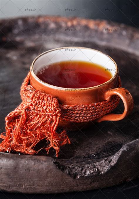 عکس یک فنجان چای و یک شال گردن که به دور آن بسته شده است روی سینی مشکی