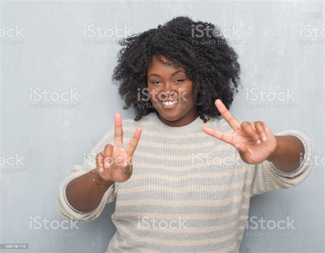 젊은 아프리카계 미국인 플러스 크기 여자는 스웨터 웃는 찾고 승리 하 고 손가락을 보여주는 카메라 입고 회색 그런 지 벽에 서명 합니다 번호 2입니다 가을에 대한 스톡 사진