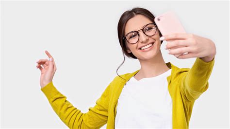 흰색 스튜디오 벽에 자기 초상화를 복용 캐주얼 옷에 예쁜 젊은 유럽 여자 행복 한 여자 웃 고 그녀의 스마트 폰에 Selfie을