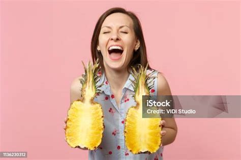 분홍색 파스텔 배경에 고립 된 신선한 파인애플 과일의 Halfs를 들고 눈을 유지 하는 여름 옷에 젊은 여자를 웃 고 사람들은 생생한 라이프 스타일 휴식 휴가 개념입니다