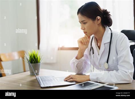 An Asian Female Doctor Uses A Computer While Showing Concern About