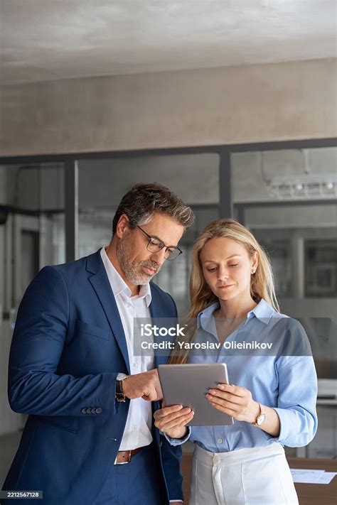 성숙한 고위 리더 양복을 입은 남자와 사무실에 서있는 태블릿에서 프로젝트를 논의하는 젊은 직원 여성의 팀 스크린 장치를 보고 있는 전문 사업가의 두 동료 세로 25 29세에