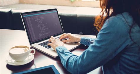 caucasian female programmer sitting at desk with coffee using laptop