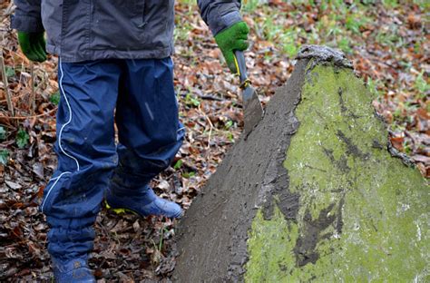 진흙 시멘트 석고와 벽을 던지는에 재생 어린 소년 그들은 아빠에게서 도구를 빌렸습니다 주걱 타일 접착제처럼 진흙을 얼룩 군사 장애물 콘크리트 피라미드 숲에서 가을에 대한