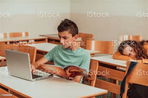 학교 교실에 앉아 있는 한 소년이 책을 손에 들고 노트북을 사용합니다 선택적 초점 Brand Name Smart Phone에 대한 스톡 사진 및 기타 이미지 Brand