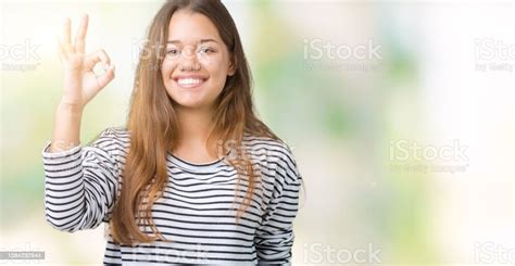 젊은 아름 다운 갈색 머리 여자 격리 된 배경 손과 손가락으로 Ok 사인을 하 고 긍정적인 미소에 줄무늬 스웨터를 입고 성공적인