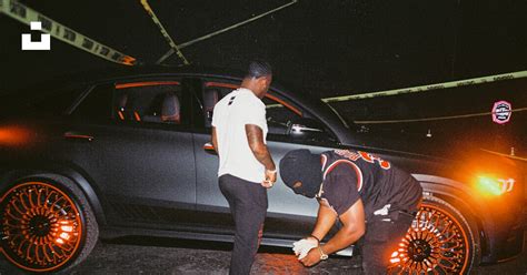 흰색 티셔츠와 검은 바지를 입은 남자가 검은 차에 기대어 있다 사진 Unsplash의 무료 미국 이미지