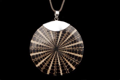 A Circular Pendant Of Black And Cream Natural Patterned Shell Slices Set On A Black Resin Base