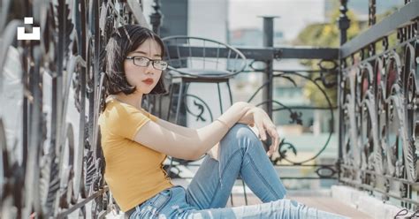 노란색 셔츠와 파란색 데님 청바지를 입은 여자가 낮에 회색 금속 벤치에 앉아 있다 사진 Unsplash의 무료 회색 이미지