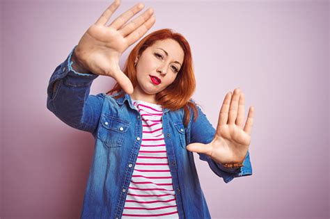 아름다운 빨간 머리 여자 데님 셔츠와 스트라이프 티셔츠 를 입고 고립 된 분홍색 배경 위에 손을 손바닥과 손가락을 사용하여 프레임을하고 카메라 관점 T 셔츠에 대한 스톡