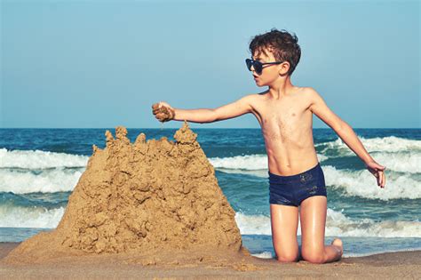 아이는 젖은 모래에서 모래 성을 빌드합니다 선글라스에 있는 소년은 석양에 밝은 여름 날에 장난감 해변에서 재생 됩니다 관광
