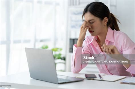 안경을 들고 열심히 생각하는 아시아 사업가는 눈 주위에 통증이 있다 사무실에서 노트북 화면을 보면서 온라인 문서 데이터를