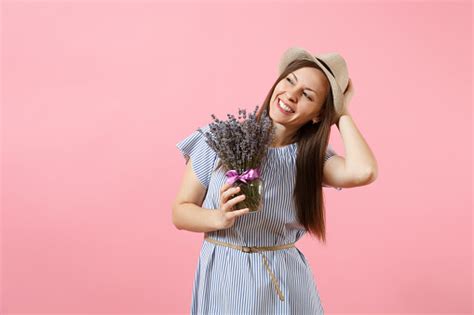 블루 드레스를 입고 모자 밝은에 고립 된 아름 다운 보라색 라벤더 꽃의 꽃다발을 들고 행복 한 젊은 부드러운 여자의 핑크 배경
