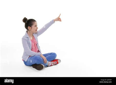 A Young Girl Sitting Cross Legged On The Floor And Pointing At
