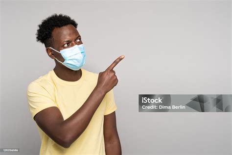 진지한 Afroamerican 남자는 두 개의 집게 손가락으로 얼굴 마스크 포인트를 착용하고 광고를위한 빈 복사 공간을 보여주며