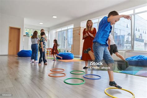 작은 보육원 아이들 교실에서 실내 바닥에 여성 교사와 함께 운동을하고 훌라 후프 서클을 뛰어 넘으면 바닥에서 추적됩니다