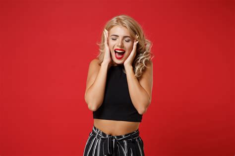 빨간 배경 스튜디오 초상화에 고립 된 포즈 검은 옷을 입고 기뻐하는 젊은 여성 소녀 사람들은 진지한 감정 라이프 스타일 개념 복사 공간을 모의합니다 눈을 감고 뺨에 손을