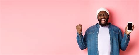 스마트폰 화면을 보여주는 온라인 성과를 축하하는 행복한 흑인 남자 무료 사진