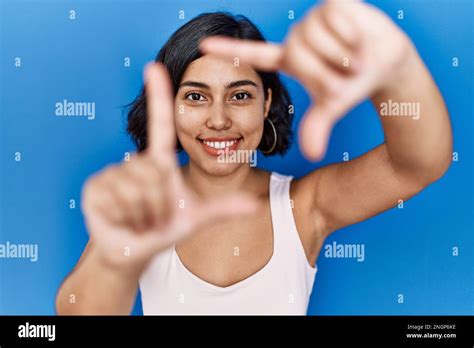 Young Hispanic Woman Standing Over Blue Background Smiling Making Frame