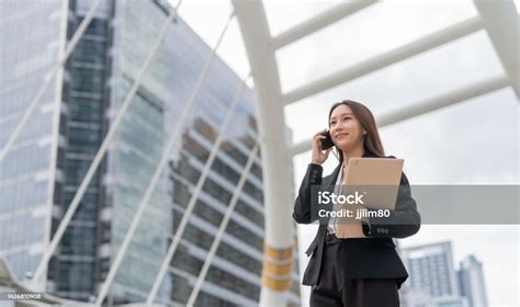 매력적인 젊은 아시아 전문 사업가 숙녀 그녀의 얼굴에 좋은 미소를 지으며 방콕 도시의 중심 비즈니스 지구에서 클립 폴더 보드를 걷고 들고있는 동안 전화로 이야기합니다 25