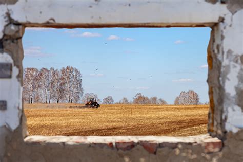 맑은 봄 날 푸른 하늘 아래 노란 색의 농업 산업에 대 한 깎고 및 잡 초 필드에 대 한 개척 쟁기와 트랙터에 건물의 옛 파괴 창에서 보기 심기 각도에 대한 스톡 사진 및