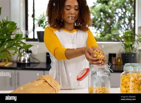 Happy biracial woman pouring pasta from hands into storage jar in kitchen Stock Photo - Alamy