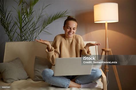 노트북으로 소파에 앉아있는 캐주얼 한 옷을 입고 화상 통화를하거나 라이브 스트림을 방송하고 어깨를 으쓱하고 확실하지 않은 무력한 백인 여성의 수평 촬영 30 34세에 대한