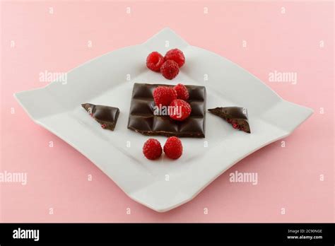 Dark Chocolate Candy Bar With Bits Of Raspberry And Fresh Raw Red Raspberries On White Dessert