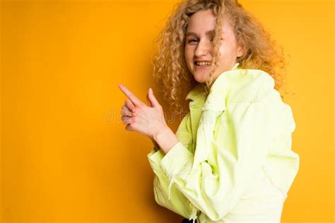 A Cute Young Girl With Curly Hair Stands Sideways And Puts Her Index