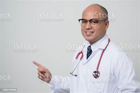 흰색 코트를 입은 의사 청진기 가리키는 손가락 옆에 카메라로 들여다 보십시오nwith 미소와 흰색 배경에 고립 된 기울기 30