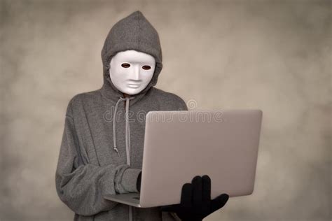Computer Hacker Wearing Hoodie Mask And Gloves Using A Laptop Stock