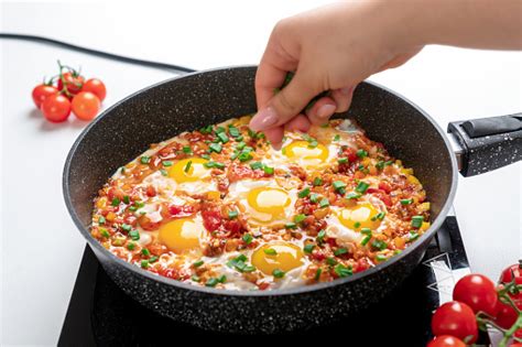 요리사는 다진 피망 토마토 양파를 곁들인 프라이팬에 스크램블 에그에 파를 넣고 스토브에서 튀깁니다 Shakshuka와